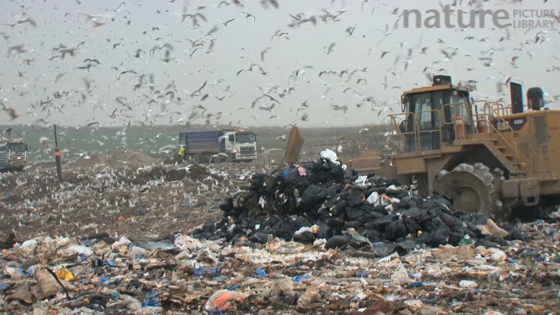 Panning shot across a landfill site with working machinery and mixed ...